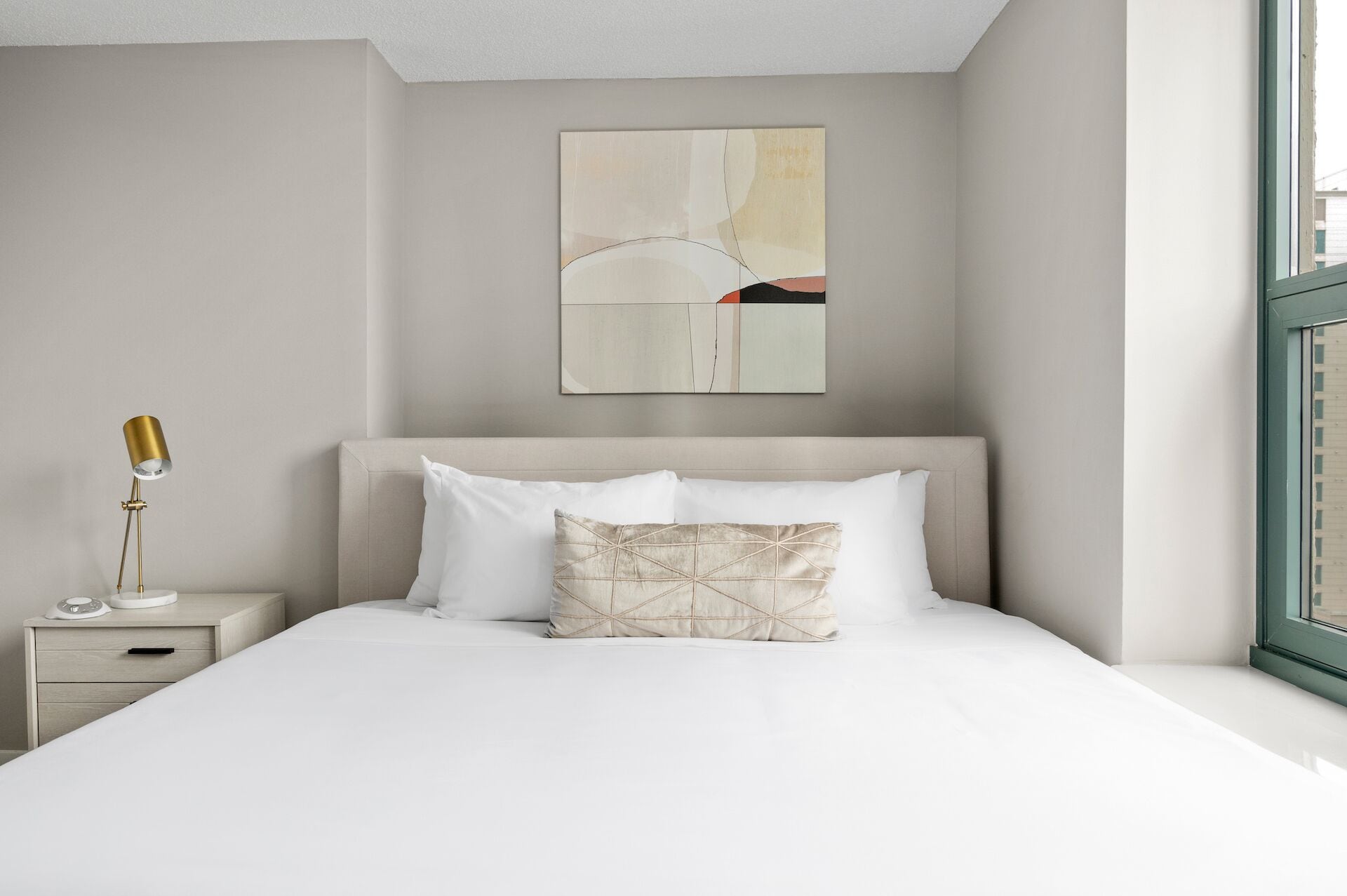 Quarto moderno com uma cama grande, mesa de cabeceira com abajur e vista para a cidade pela janela.