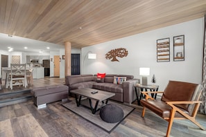 Uma sala de estar moderna com um sofá modular, uma mesa de centro, uma mesa lateral e uma obra de arte de parede com tema de árvore decorativa.