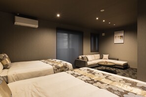 Quarto de hotel com duas camas, um sofá, uma mesa de centro e uma janela grande.