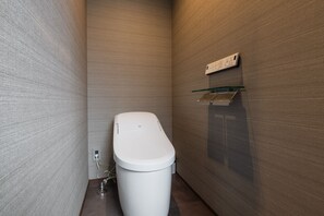 Um banheiro moderno com vaso sanitário branco, prateleira de vidro e painel de controle fixado na parede.