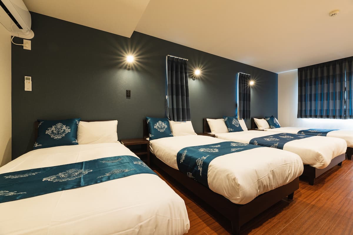 Quarto de hotel com quatro camas dispostas em linha, cada uma com colcha azul escura e roupa de cama branca.