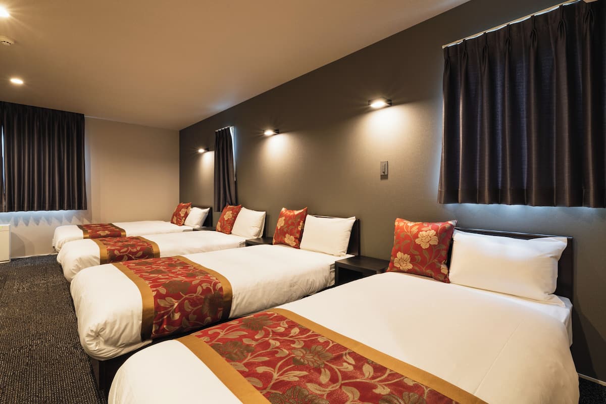Quarto de hotel com três camas, cada uma com lençóis brancos e colchas floridas vermelhas.