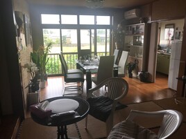 Uma sala de jantar com mesa e cadeiras, uma cozinha ao fundo e vista para o exterior.