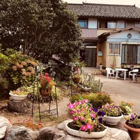 Uma casa japonesa tradicional com um jardim frontal, com plantas em vasos e uma pequena área de estar ao ar livre.
