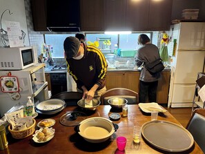 Uma cozinha com armários de madeira, micro-ondas e geladeira. Há diversos utensílios de cozinha na bancada, incluindo tigelas, um cesto e uma garrafa.