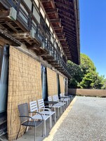 Edifício com fachada de madeira e área de estar externa coberta, com cadeiras brancas.