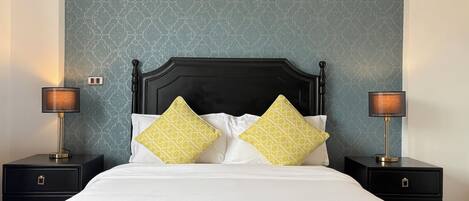 Cama com roupa de cama branca e duas almofadas amarelas estampadas, com mesas de cabeceira pretas e luminárias.