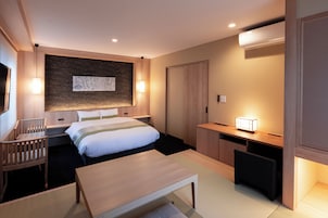 Quarto de hotel moderno com cama, escrivaninha, cadeira e mesa de cabeceira.