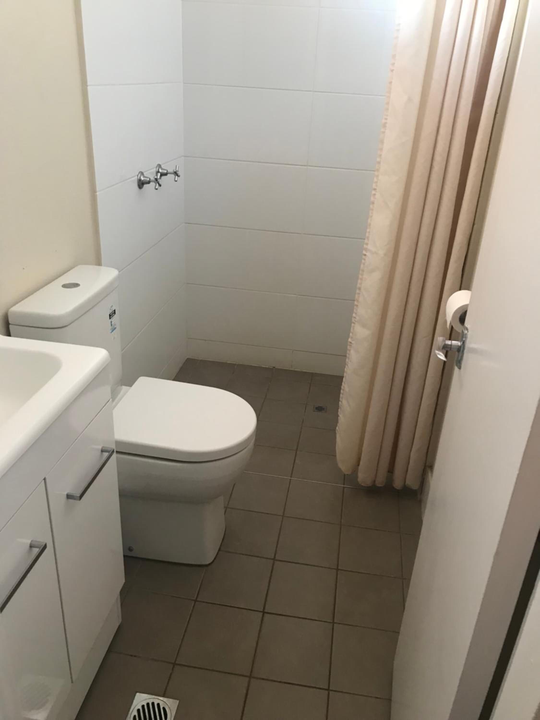 Casa de banho pequena e limpa, com sanita, lavatório e cortina de chuveiro.