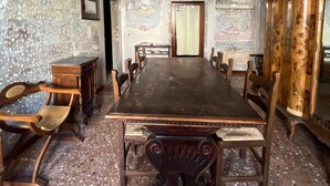 Um quarto com uma mesa de madeira grande, várias cadeiras, um armário de madeira e uma porta que dá para outro cômodo.