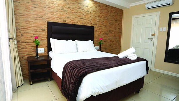 Quarto de hotel com uma cama grande, uma mesa de cabeceira com um vaso de flores e um revestimento de parede em tijolos.