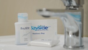 Uma pia de banheiro com uma torneira, uma embalagem de Bayside body wash, um saco sanitário e uma barra de sabão.