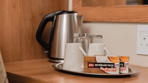 Uma bandeja com um kit de bebidas, duas xícaras brancas e uma chaleira de prata sobre uma mesa de madeira.