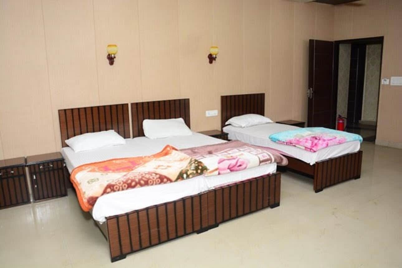 Quarto de hotel com duas camas, cada uma com cabeceira de madeira e roupa de cama branca. Há duas luminárias fixadas na parede e uma porta com espelho.
