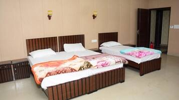 Quarto de hotel com duas camas, cada uma com cabeceira de madeira e roupa de cama branca. Há duas luminárias fixadas na parede e uma porta com espelho.