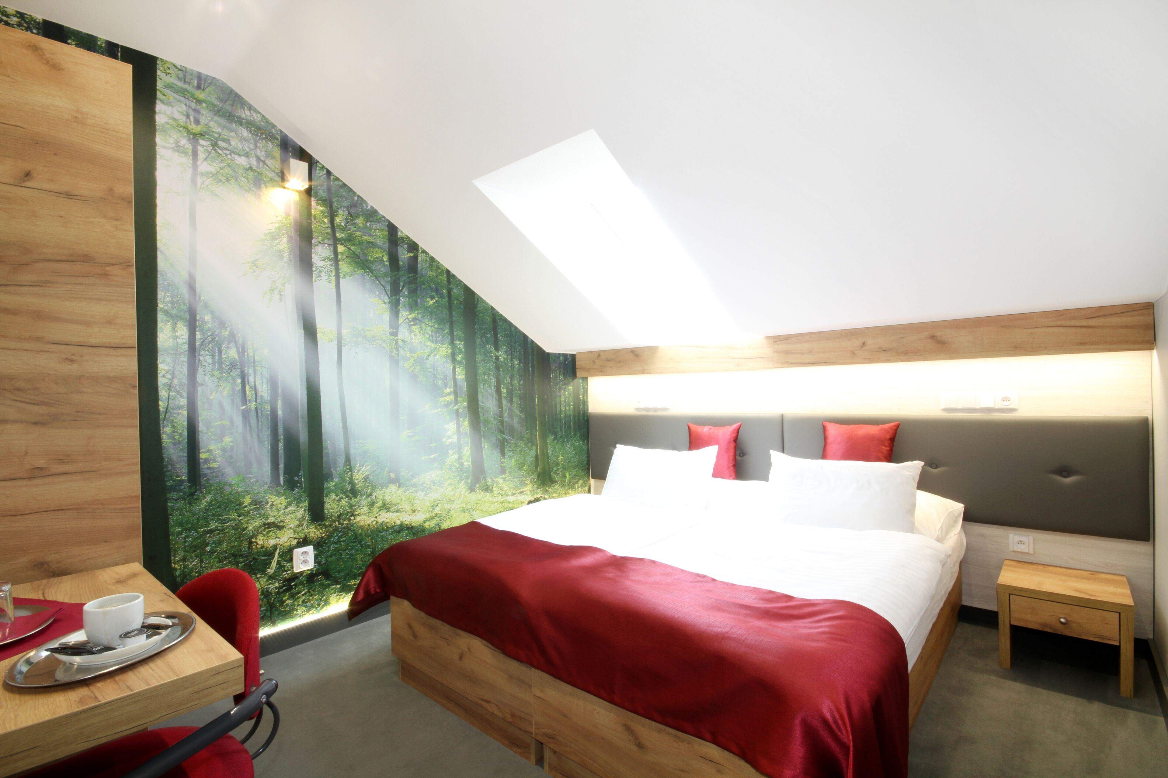 Um quarto com uma cama grande, uma escrivaninha com cadeira e vista para uma floresta pela janela.
