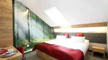 Um quarto com uma cama grande, uma escrivaninha com cadeira e vista para uma floresta pela janela.