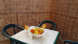 Uma mesa com uma tigela de fruta e dois copos de suco de laranja, rodeada por quatro cadeiras.