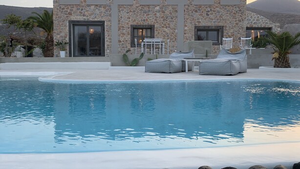 Uma área de piscina com espreguiçadeiras e um edifício de pedra com janelas amplas.