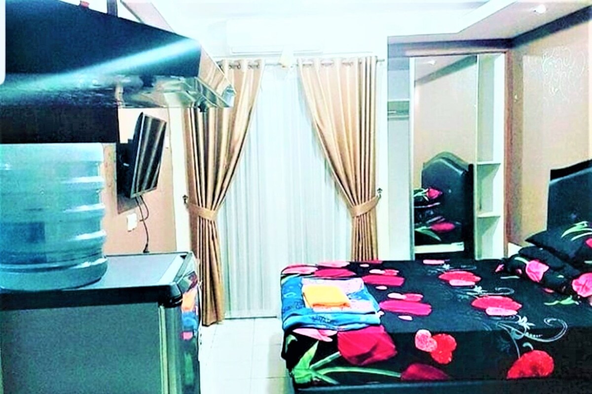 Quarto de hotel com cama, dispensador de água, televisão e porta deslizante.