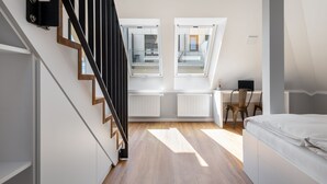 Um quarto moderno com escada de madeira, área de dormir no mezanino e uma escrivaninha com cadeira.
