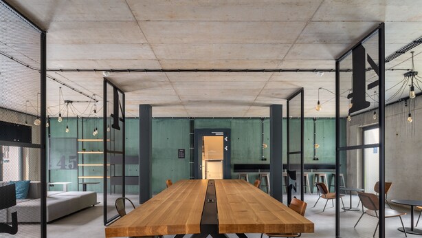 Uma sala de conferências com uma longa mesa de madeira, cadeiras de metal e teto alto com vigas aparentes.