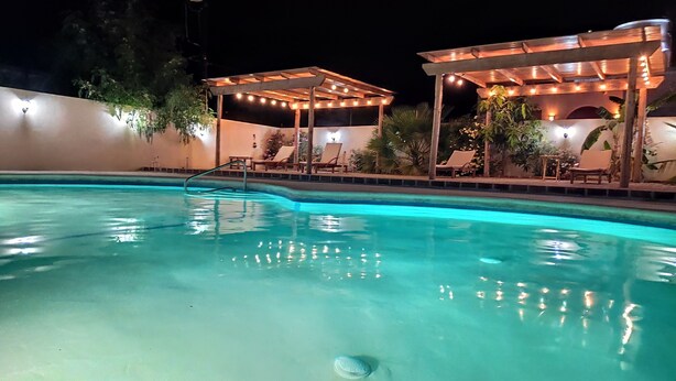 Piscina com deck de madeira e espreguiçadeiras, cercada por paredes com luzes de Natal.