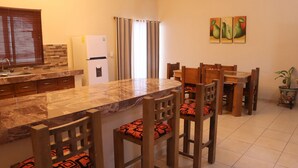 Cozinha moderna com bancada de mármore, cadeiras de madeira com almofadas estampadas, uma geladeira e uma mesa de jantar.