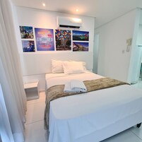 Quarto de hotel com cama, mesa de cabeceira e parede com cartazes de boas-vindas em vários idiomas.