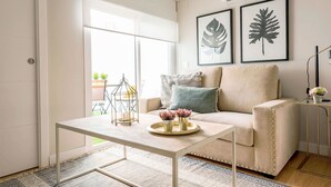 Uma sala de estar moderna com um sofá bege, uma mesa de centro com objetos decorativos e duas obras de arte com folhas emolduradas na parede.