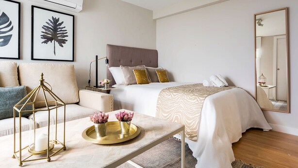 Quarto moderno com cama, mesa de cabeceira, abajur e um espelho grande.