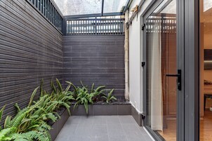 Um espaço exterior moderno com uma parede de madeira escura, uma porta de vidro e chão ladrilhado.