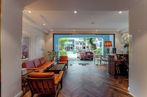Um quarto amplo com piso de madeira em padrão herringbone, um sofá de couro e uma escrivaninha com abajur.