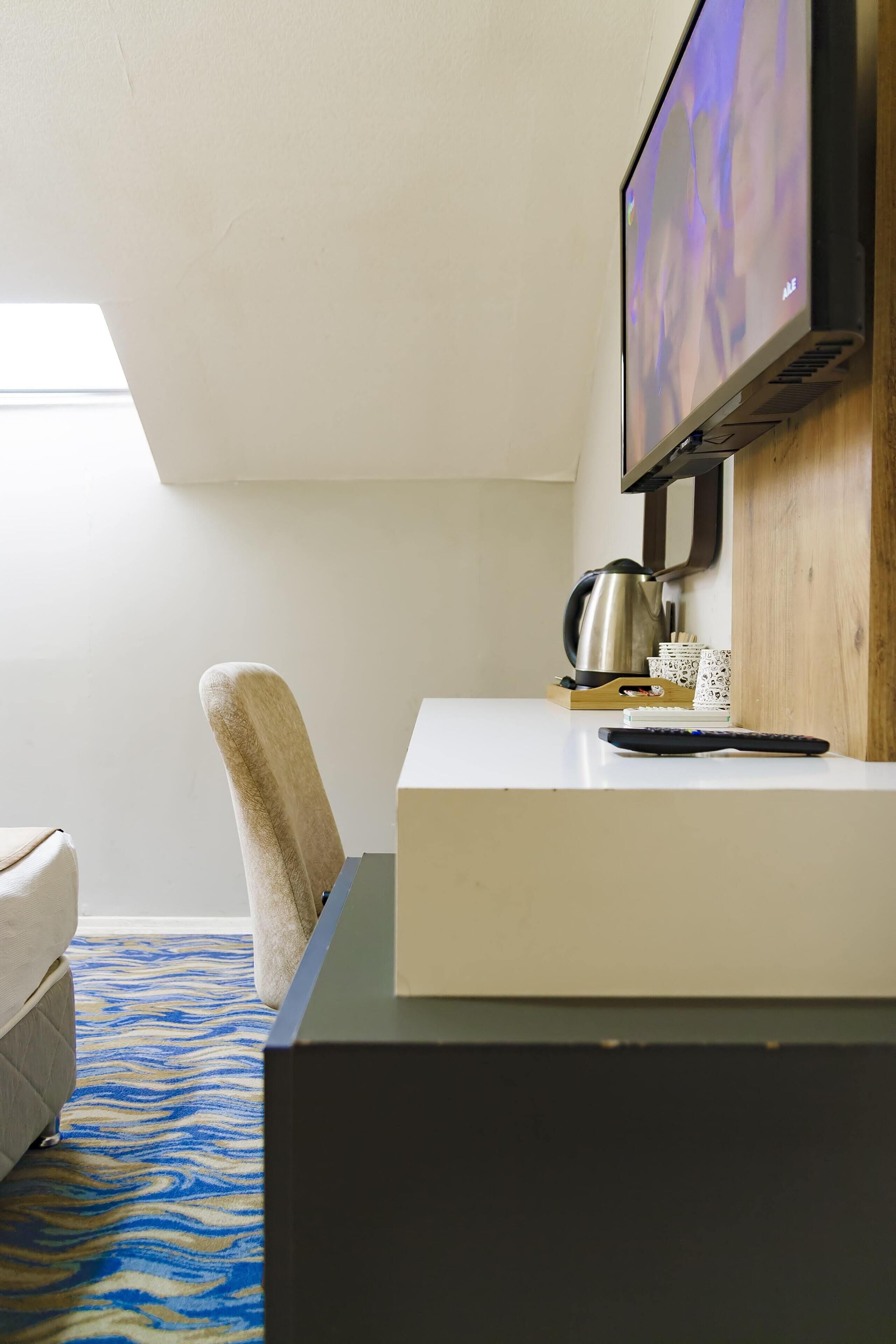 Quarto de hotel moderno com uma secretária branca, uma TV de tela plana na parede, chaleira e cafeteira.