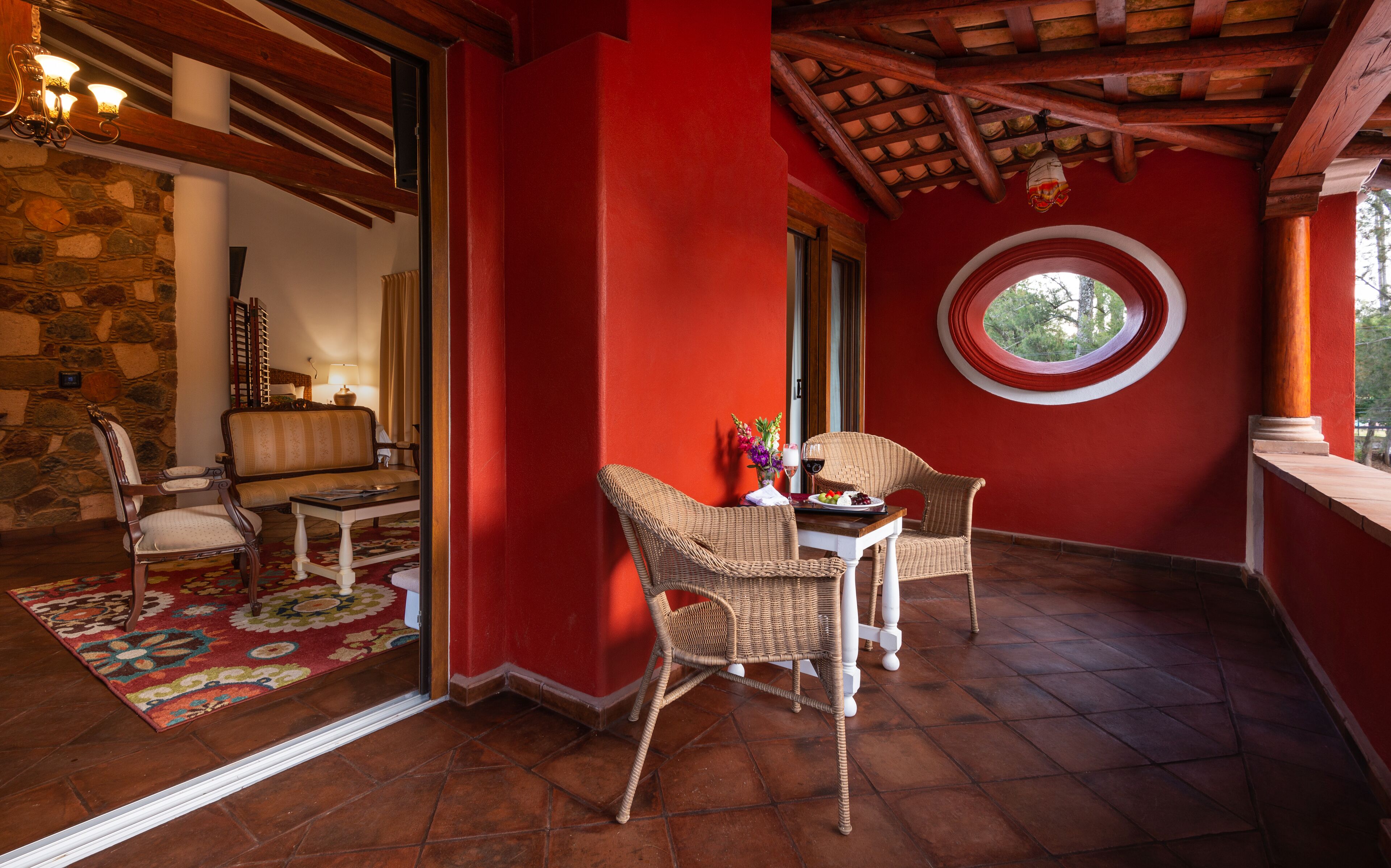 Um quarto com paredes vermelhas, cadeiras de vime, uma mesa e uma janela.