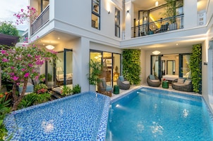 Um hotel moderno com uma grande piscina interna, várias varandas e vegetação exuberante.