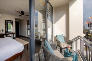 Quarto de hotel com cama, escrivaninha, móveis de vime e varanda com guarda-corrimão.