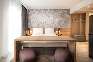Quarto de hotel moderno com cama de madeira, uma pequena mesa, duas cadeiras, parede estampada e guarda-roupa com espelho.