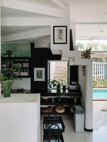 Uma cozinha moderna com painel de parede preto, bancadas brancas e vista para a piscina ao ar livre.