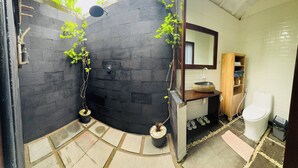 Um banheiro com parede revestida de azulejos pretos, um armário de madeira, uma pia e um vaso sanitário.