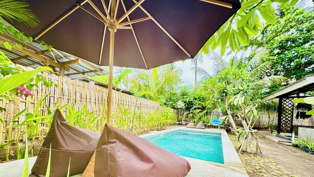 Uma área de piscina com deck de madeira, uma cadeira suspensa e um grande guarda-sol para dar sombra.