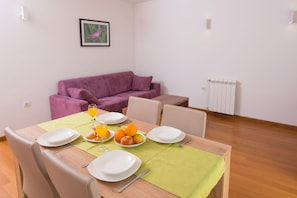 Uma área de refeições com uma mesa posta para dois, um sofá roxo e um radiador na parede.