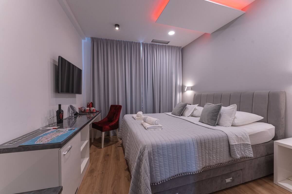 Quarto de hotel moderno com cama, escrivaninha, cadeira e televisão.
