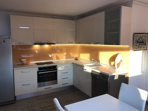 Uma cozinha moderna com armários brancos, forno embutido, máquina de lavar louça e uma mesa de jantar branca com cadeiras.
