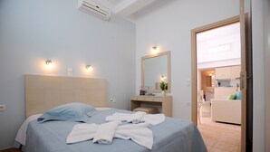 Quarto de hotel com cama, mesa de cabeceira, espelho e vista para a cozinha.
