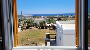 Vista da janela com vista para uma área costeira, com edifícios, céu claro e mar ao longe.