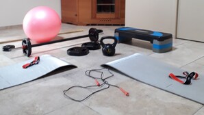 Quarto com equipamento de ginástica, incluindo um kettlebell, faixas de resistência e um tapete de yoga.