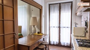 Quarto com escrivaninha de madeira, luminária, dois banquinhos de vime, espelho grande e janela com cortinas leves.