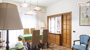 Uma área de refeições com uma mesa, cadeiras e uma luminária. Há uma porta e um quadro na parede.