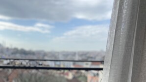 Uma varanda com mesa e cadeiras, uma tigela de frutas e vista para edifícios ao longe.
